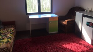 A room with a desk, a chair, a bed, and a window.