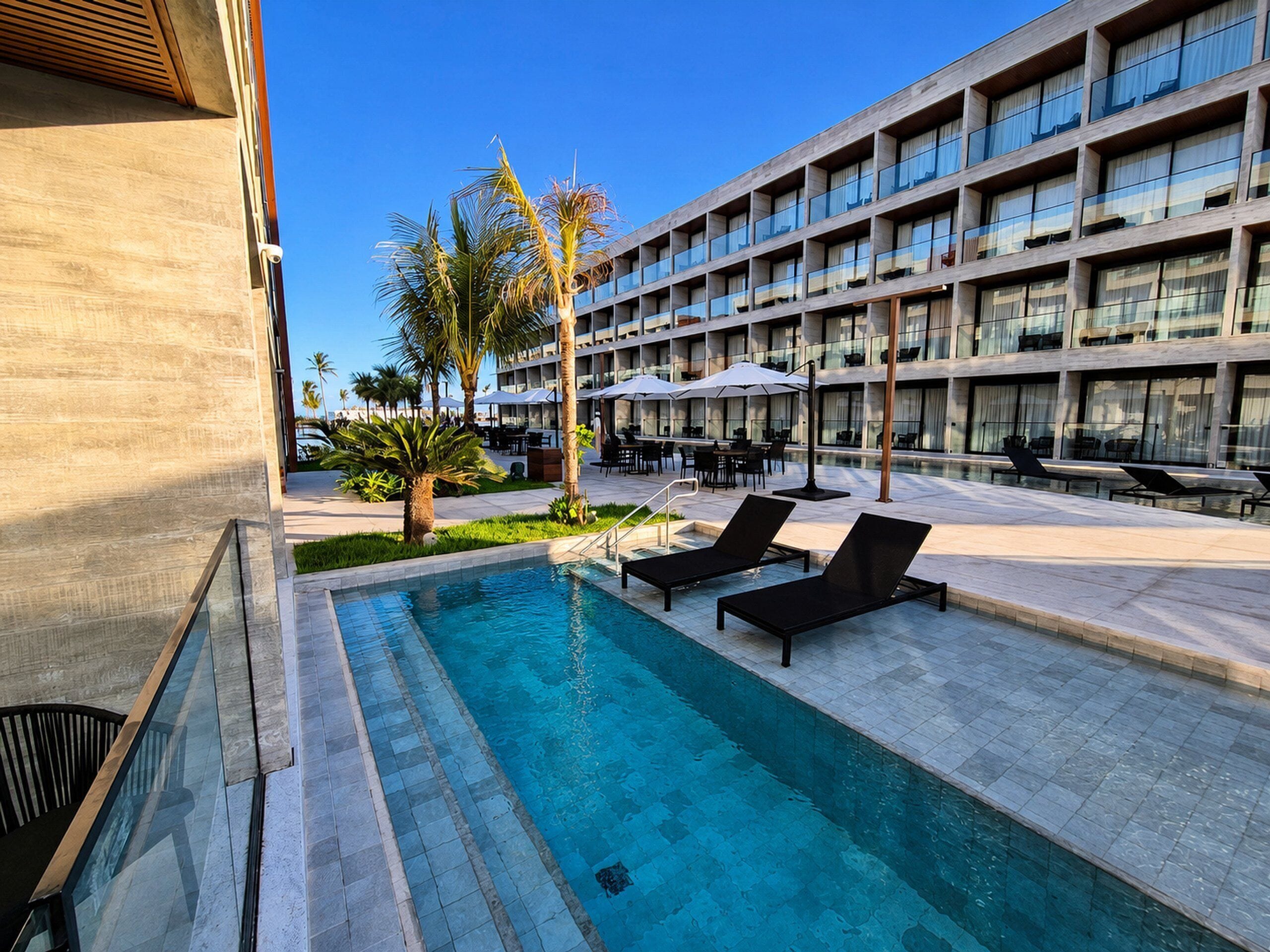 Uma área de piscina de hotel com espreguiçadeiras, uma piscina e um edifício com várias varandas.