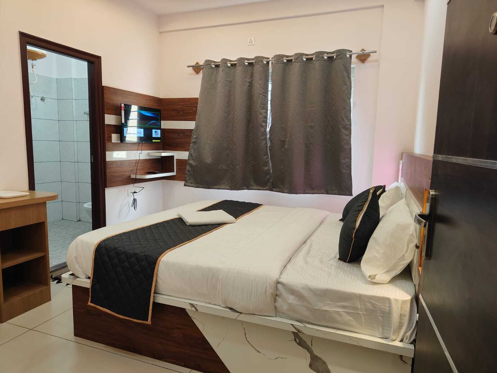 Quarto de hotel com uma cama, televisão fixada na parede, banheiro com chuveiro e uma porta com cortina.
