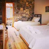 Quarto com duas camas, uma mesa de madeira e uma parede de pedra.