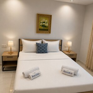 Cama bem arrumada com duas toalhas, um quadro na parede e abajures.