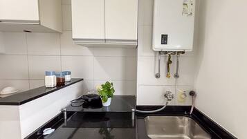 Uma cozinha compacta com bancada preta, pia de aço inoxidável e aquecedor à água fixado na parede.
