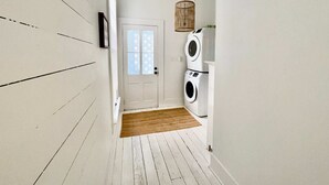 Uma lavanderia com uma porta, duas máquinas de lavar empilhadas e piso de madeira.