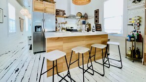 Uma cozinha moderna com uma ilha central, banquetas, luminária pendente e garrafas de vinho na parede.