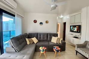 Uma sala moderna com um sofá seccional cinza, uma TV de tela plana na parede e um ventilador de teto.