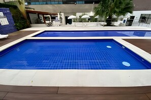 Piscina com deck revestido e área de estar coberta com guarda-sóis.