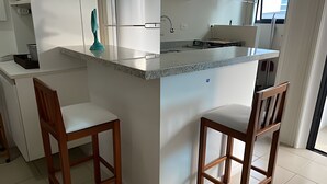 Cozinha com ilha central, dois banquetes de madeira, armários brancos e janela que traz luz natural.