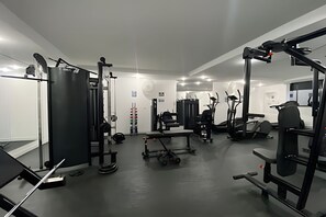Uma academia com diversos equipamentos de exercícios, incluindo um suporte para agachamento, aparelho de supino e esteiras.