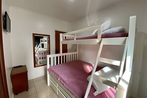 Quarto com beliche, escrivaninha e guarda-roupa, além de uma janela.
