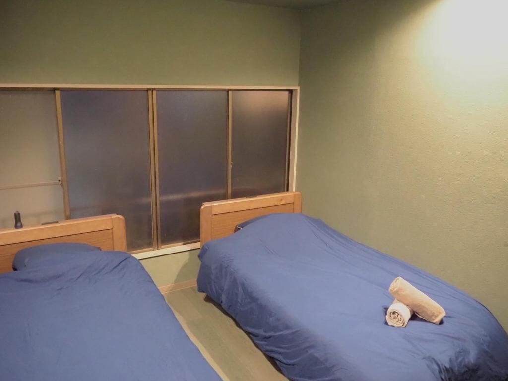 Quarto com duas camas de solteiro, uma cabeceira de madeira e uma pequena mesa de cabeceira.