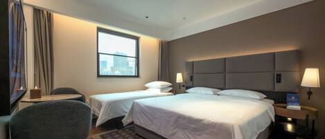 Quarto de hotel com duas camas, uma escrivaninha, uma cadeira, janela com vista e abajur na mesa de cabeceira.