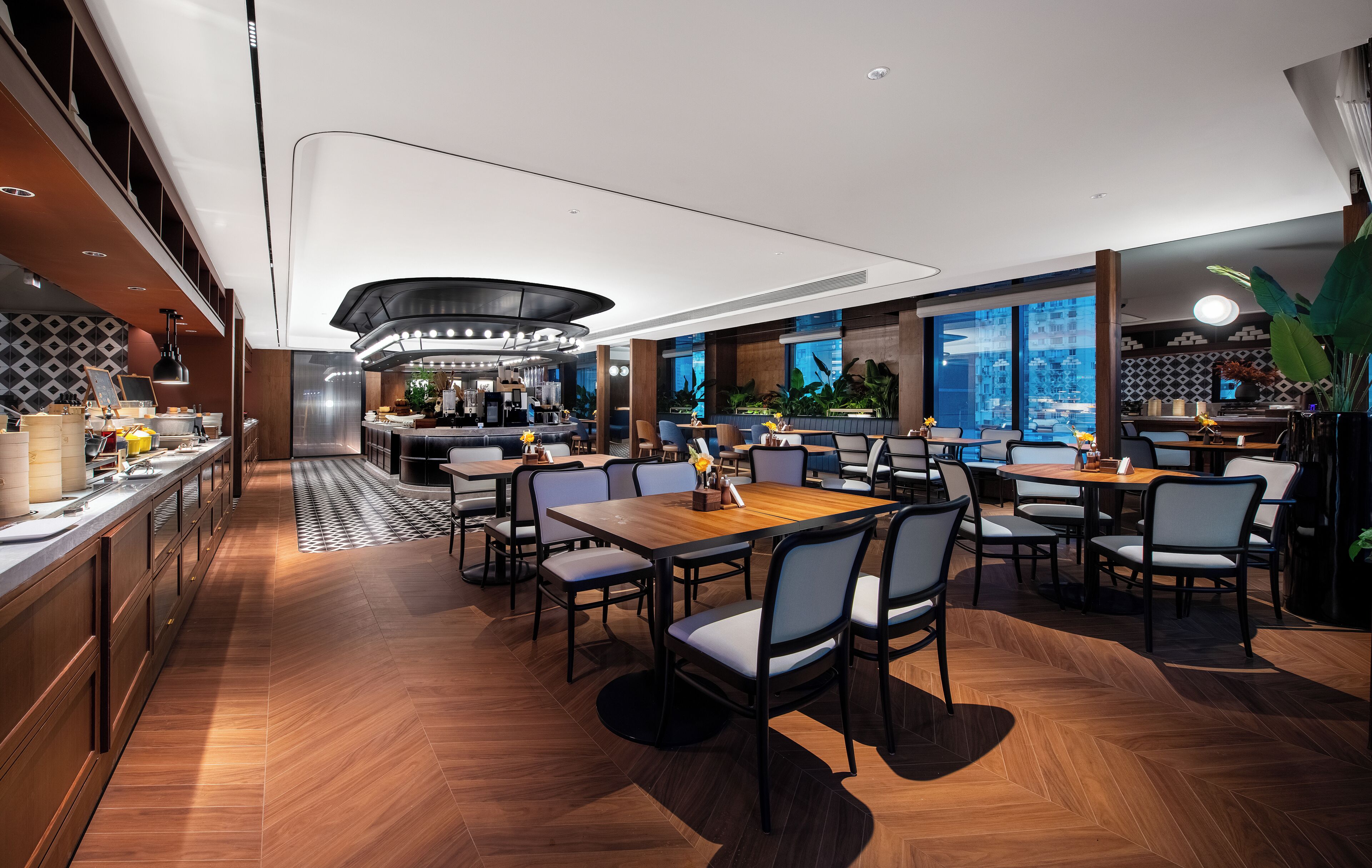 A modern restaurant with a central bar area, multiple dining tables, and a view of the cityscape through large windows.