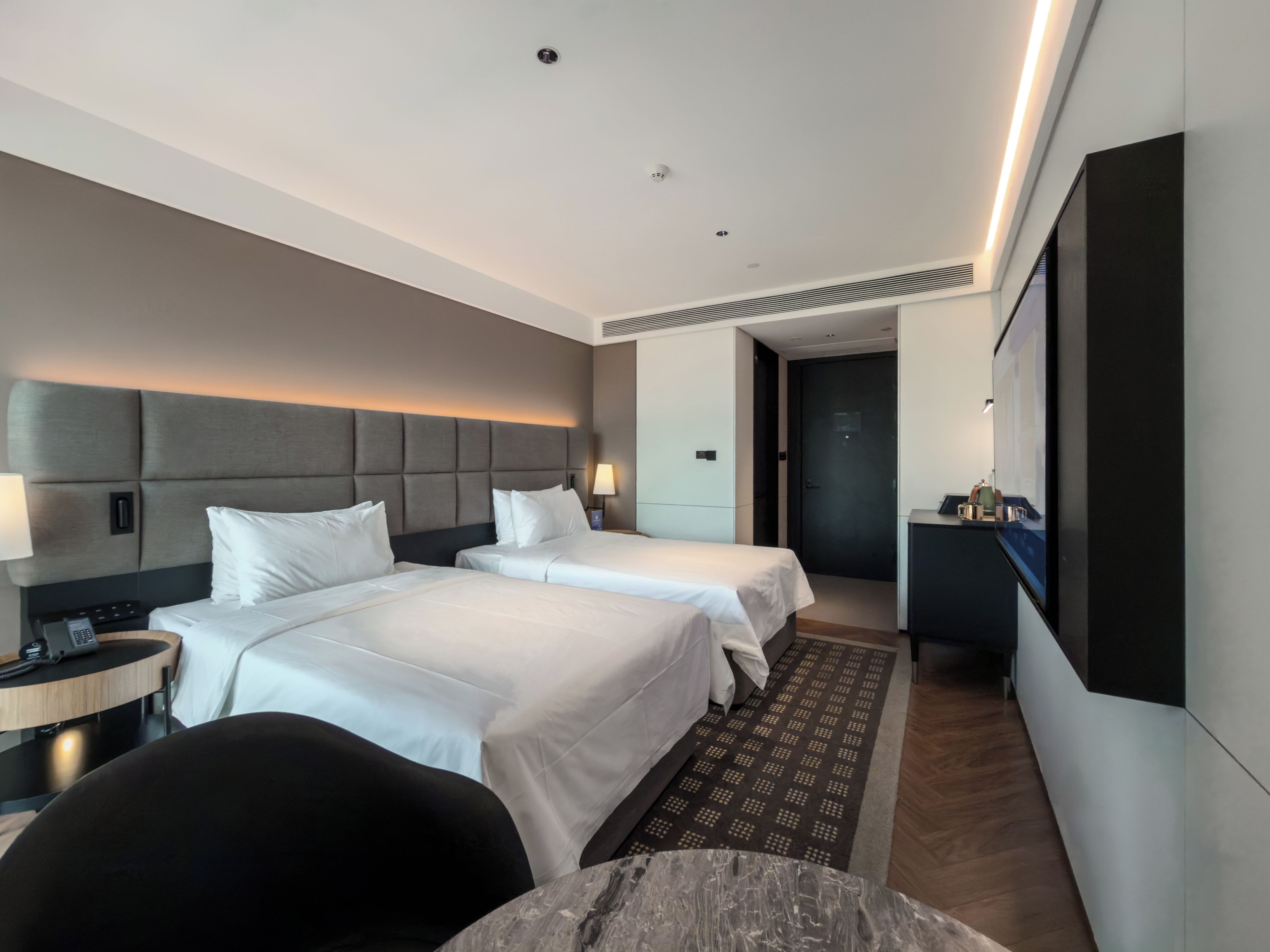 Quarto de hotel com duas camas, uma escrivaninha, uma cadeira, uma televisão e porta de banheiro.