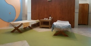 Um quarto com duas macas de massagem, uma mesinha com um bule de chá e um armário de madeira.