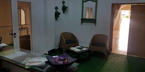 Quarto com mesa de vidro, duas cadeiras de vime, um espelho e porta para outro cômodo.