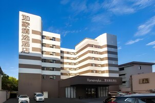 Um hotel com vários andares e design moderno, com uma placa em destaque para 'Homeinnplus' e um céu azul ao fundo.