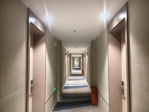 Corredor de hotel com portas em ambos os lados, piso coberto por carpete e uma lixeira no centro.