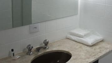 Casa de banho com lavatório, espelho, toalha e chuveiro.