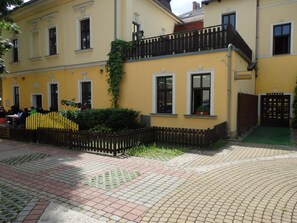 Um edifício amarelo com área de recepção, janelas e cerca de madeira.