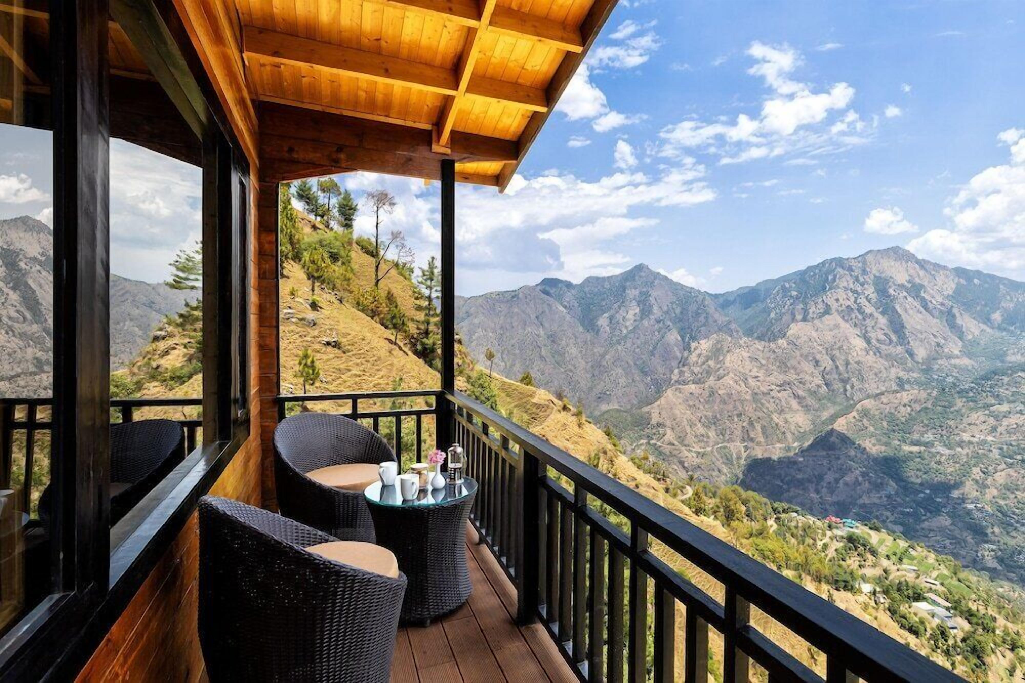 Varanda com mobiliário de vime e uma mesa, com vista para uma paisagem montanhosa.