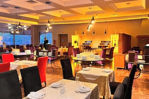 Um restaurante com várias mesas montadas para refeições, iluminação pendente e vista para o exterior.