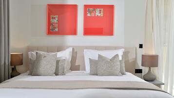 Quarto de hotel com uma cama, duas luminárias de cabeceira, uma janela com cortinas e dois quadros na parede.