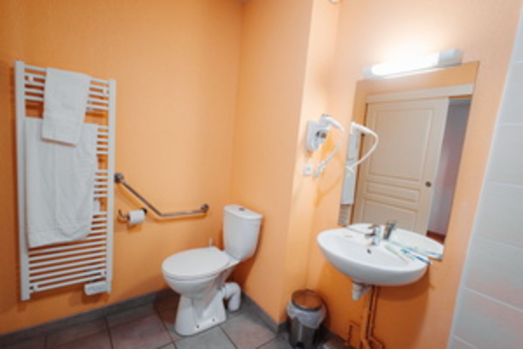 Casa de banho com sanita branca, lavatório e barra de apoio.