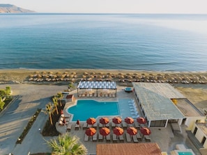 Um resort com piscina, espreguiçadeiras, guarda-sóis e vista para o mar.