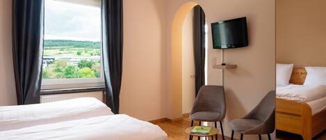 Quarto de hotel com duas camas, uma televisão presa à parede e vista para o exterior.