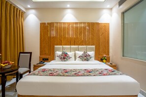 Quarto de hotel com uma cama grande, cabeceira de madeira, mesas de cabeceira, uma cadeira e uma janela.