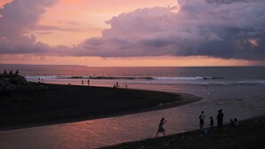 Uma praia com pessoas, uma linha costeira curva e um pôr do sol.