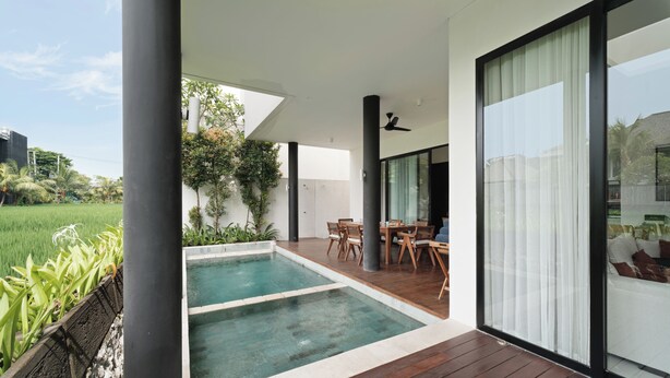 Uma área moderna de piscina ao ar livre, com um deck de madeira, uma mesa de jantar com cadeiras e uma grande porta de vidro deslizante.