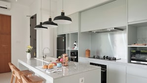 Uma cozinha moderna com uma ilha central, banquetas, iluminação pendente e eletrodomésticos de aço inoxidável.