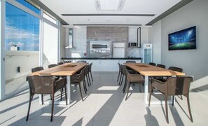 Uma sala de reuniões moderna com uma mesa comprida, cadeiras, espaço de cozinha e uma janela grande.