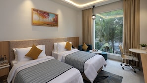 Quarto de hotel com duas camas, uma escrivaninha, uma cadeira, uma janela com cortinas e um quadro na parede.