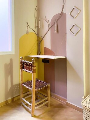 Quarto de canto com uma cadeira de madeira, uma mesa pequena e uma prateleira na parede.