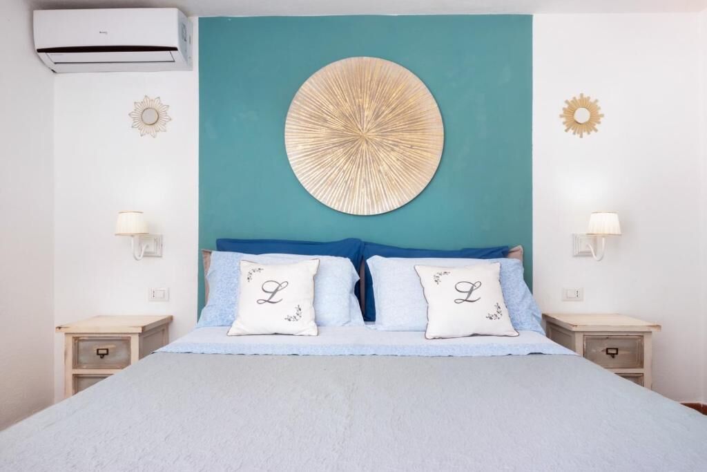 Quarto com cama, duas mesas de cabeceira, ar condicionado na parede e decoração nas paredes.