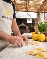 Uma pessoa preparando comida, especificamente massa, em uma cozinha com forno de tijolos e limões frescos ao fundo.