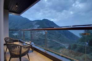 Varanda com vista para uma paisagem montanhosa, mobiliada com cadeiras de vime e uma mesa pequena.