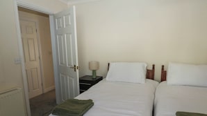 Quarto com duas camas, uma mesa de cabeceira com abajur e uma porta para outro cômodo.
