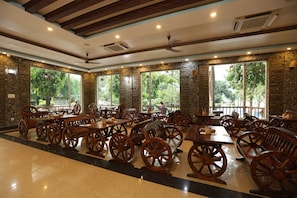Um restaurante com paredes de pedra, grandes janelas, mesas de madeira com rodízios e piso de azulejos.