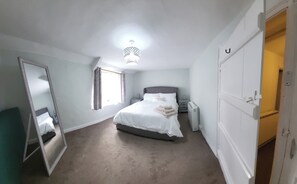 Quarto com cama, mesa de cabeceira, espelho e porta.