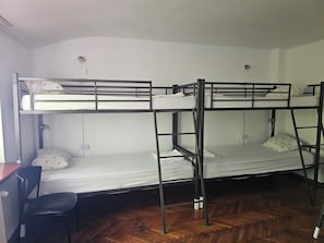 Quarto com beliche, escrivaninha, cadeira, piso de madeira e tomada na parede.