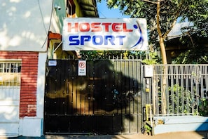 Um hostel com uma placa indicando 'HOSTEL SPORT' e uma placa de 'Proibido Estacionar'.