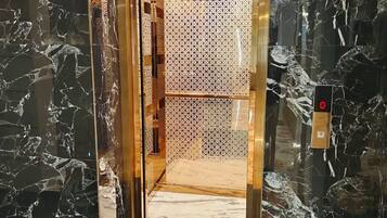 Um elevador com interior metálico refletivo, um interruptor de alarme de incêndio e uma lixeira.