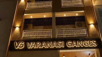Um edifício com uma placa indicando 'VG Varanasi Ganges' na entrada, com design moderno, janelas iluminadas e uma escadaria que leva ao acesso.