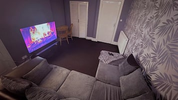 Sala de estar com televisão de tela plana, sofá, poltrona e papel de parede estampado.