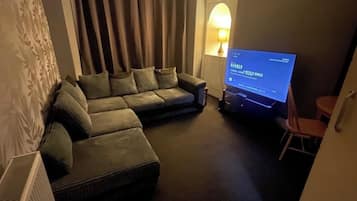 Uma sala de estar com um sofá seccional, uma televisão de tela plana e um abajur.