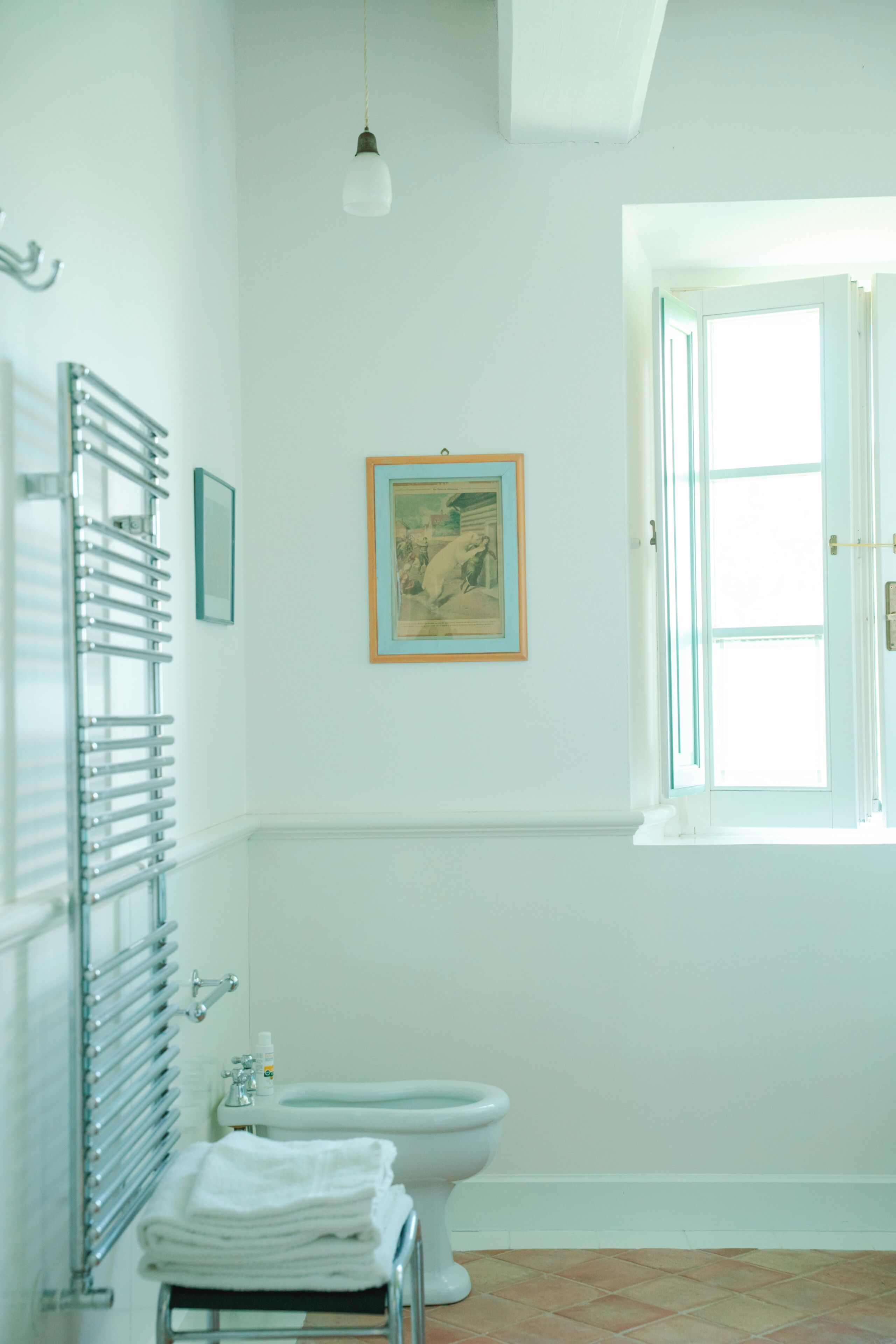 Um banheiro com vaso sanitário, porta-toalhas, um quadro na parede e uma janela.
