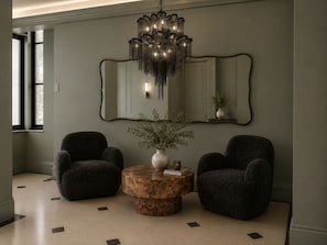 Quarto com duas poltronas, uma mesa de centro redonda, um espelho grande e um lustre.